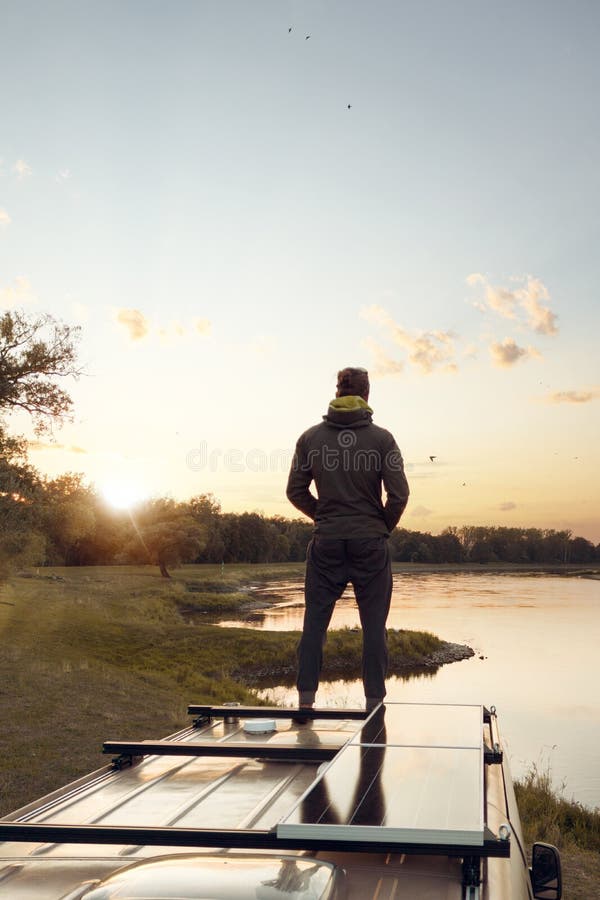 Person Standing on Top of a Camper Van Next To a River at Sunset Stock ...