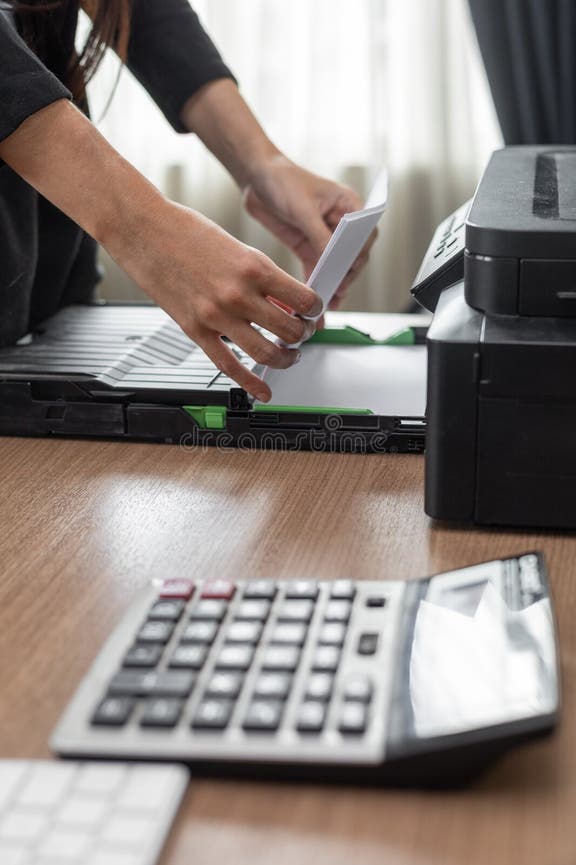 A Person Places Sheets into a Printer while a Calculator is Visible ...