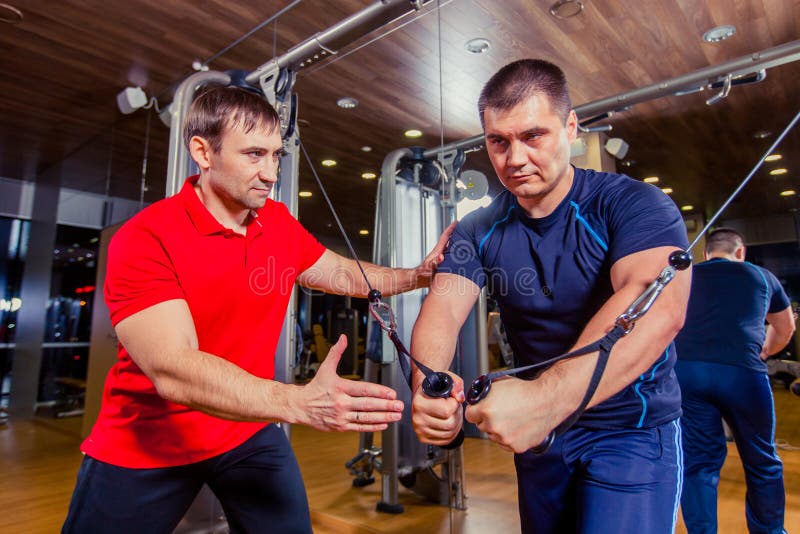 Personal Trainer Helping Men Working Out in Weights Room at the Gym ...