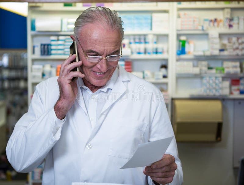 Pharmacist Talking On Mobile Phone While Checking Prescription Stock ...