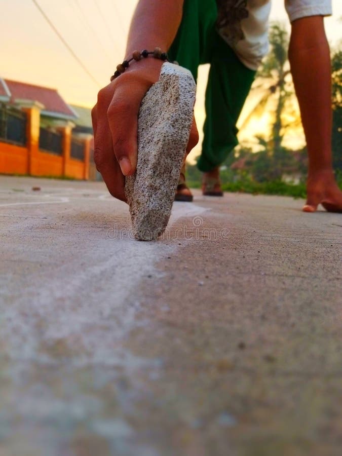A Photo of a Child Drawing on the Street Using Stones in the Evening ...