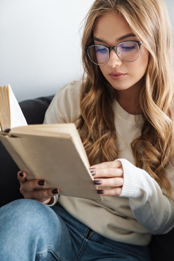 Photo Of Young Serious Woman Reading Book While Sitting On Couch Stock