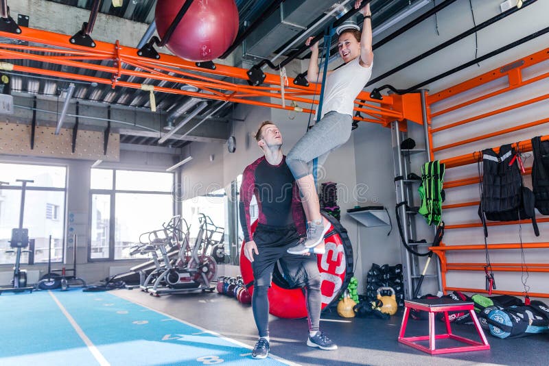 Young Woman Doing Pull-ups Under the Supervision of a Trainer Stock ...
