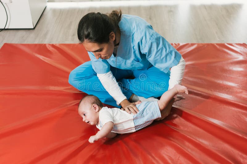 Physiotherapist Assisting Baby with Rolling Exercise on Red Mat Stock ...