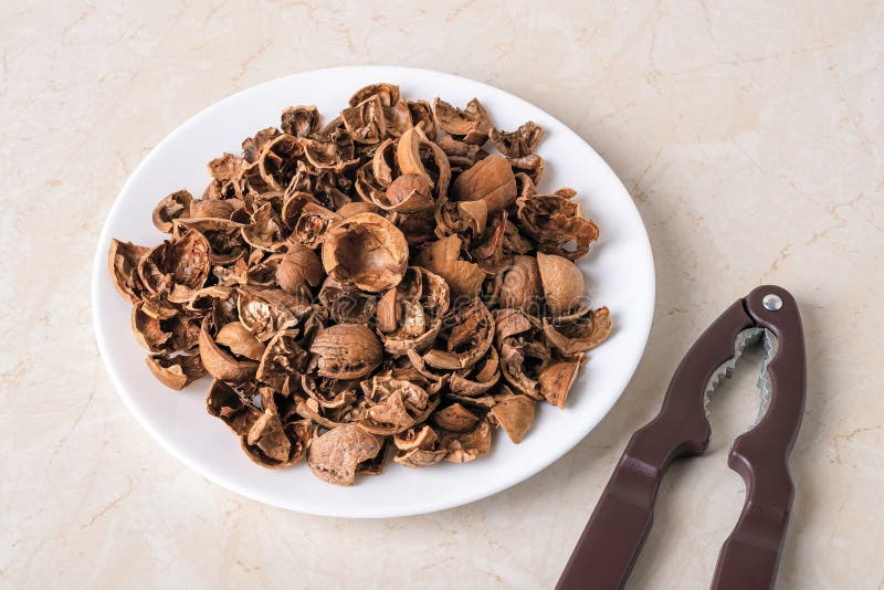 Pile of Empty Broken Walnut Shells on a White Plate and Nutcracker Over ...