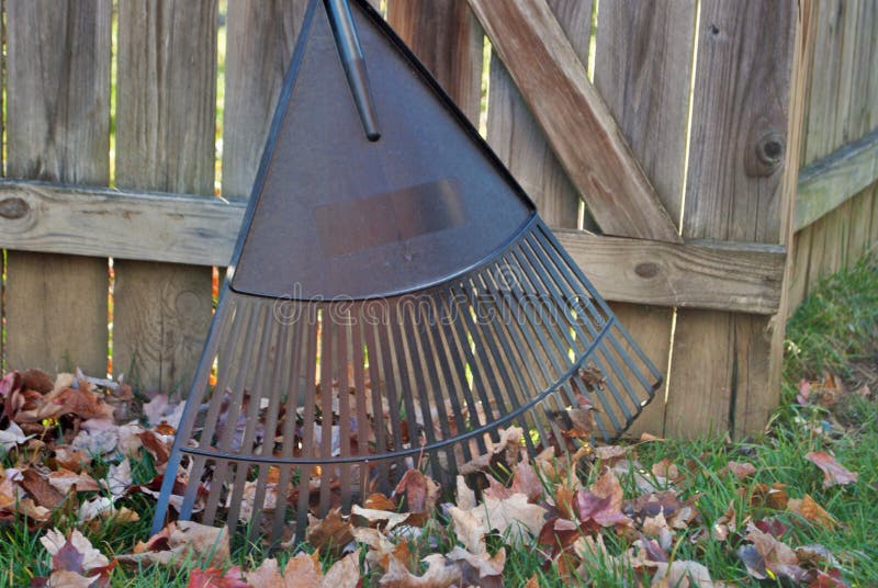 Pile of Leaves and a Rake Leaning Against a Fence Fall Background Stock ...