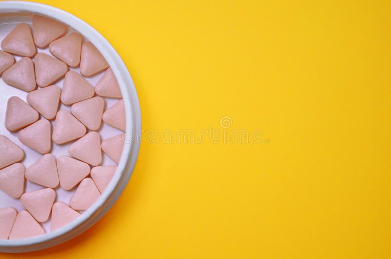 Pink Triangular Unusual Pills in a White Round Box on a Yellow ...