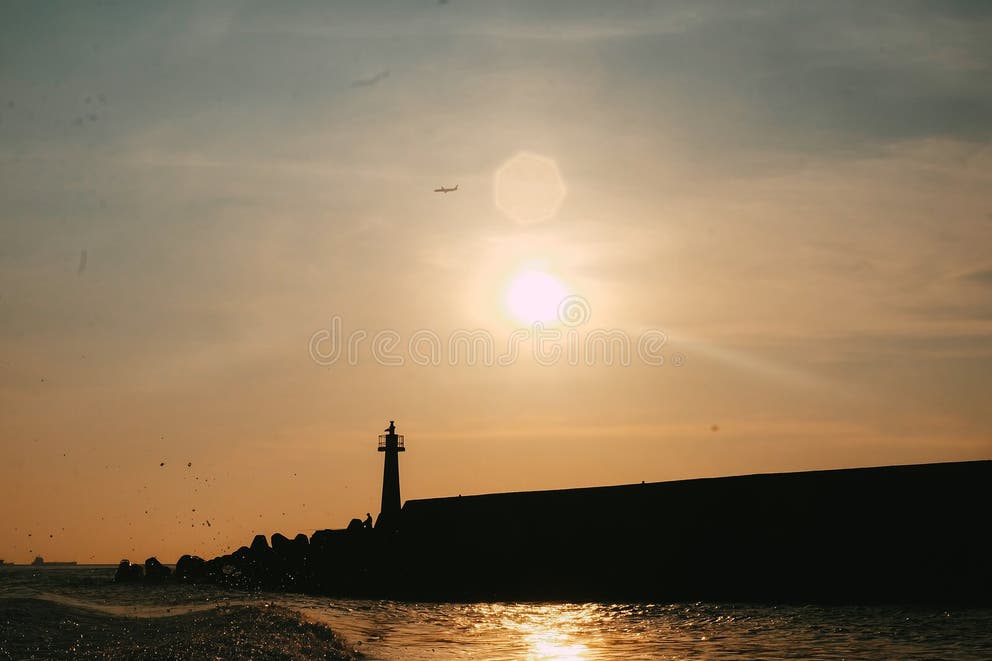 A Plane Fly Over the White Lighthouse. Lighthouse on Sunset Stock Image ...