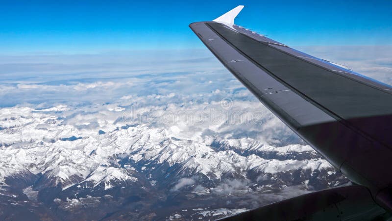 Plane Wing through an Airplane Window in Flight Trip, Snow Capped Alps ... Plane Wing through an Airplane Window in Flight Trip, Snow Capped Alps ...