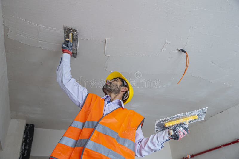 A Plasterer in Construction Wears Overalls and a Hat. he is Plastering ...