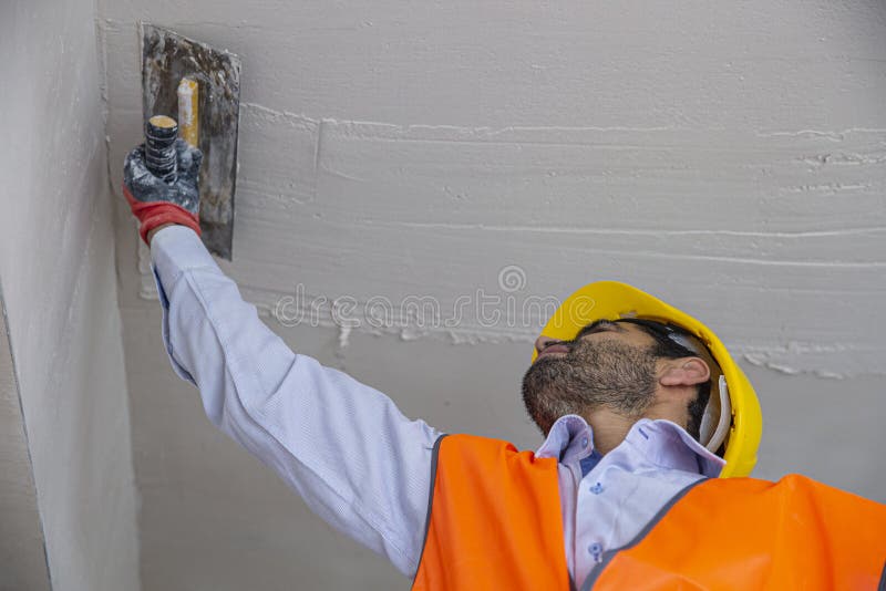A Plasterer in Construction Wears Overalls and a Hat. he is Plastering ...