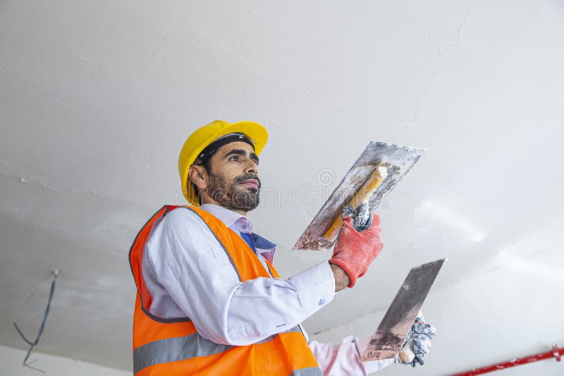 A Plasterer in Construction Wears Overalls and a Hat. he is Plastering ...