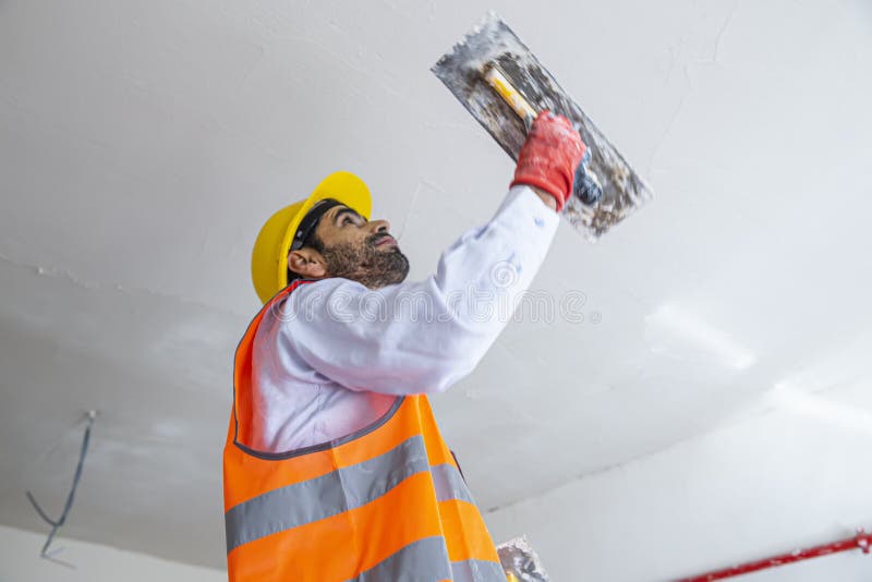 A Plasterer in Construction Wears Overalls and a Hat. he is Plastering ...