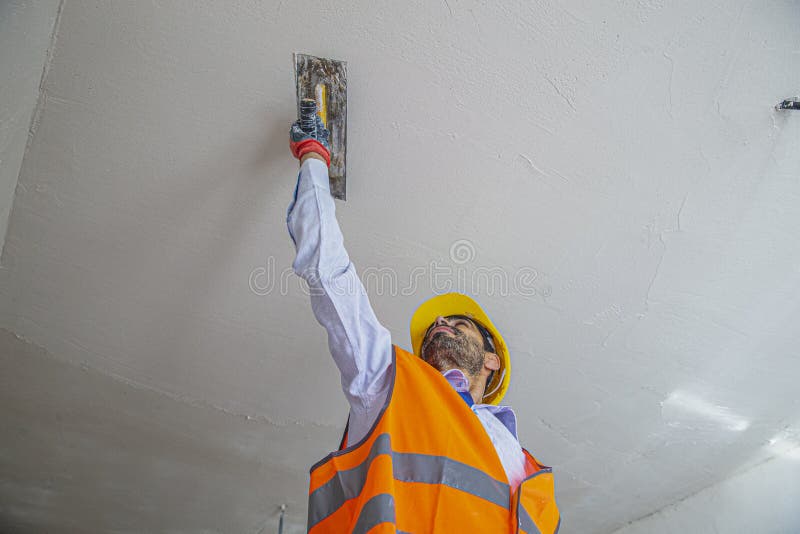 A Plasterer in Construction Wears Overalls and a Hat. he is Plastering ...