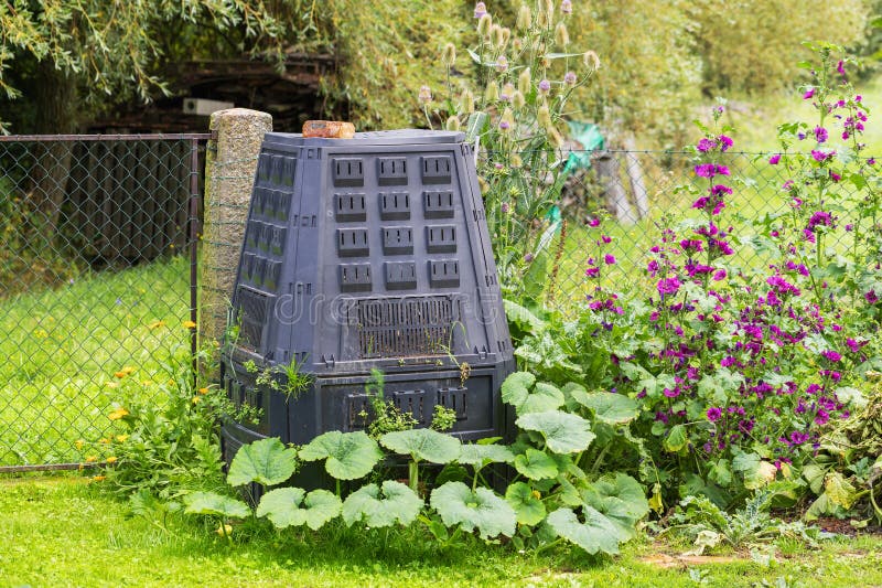 A Plastic Composter Standing by the Fence in the Garden, with Flowers ...