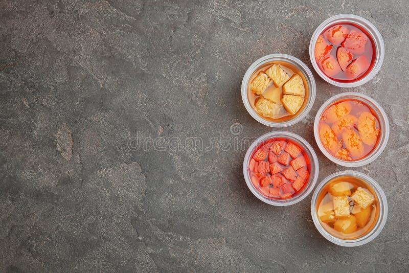 Plastic Containers of Tasty Jelly Desserts with Fruit Pieces on Grey ...