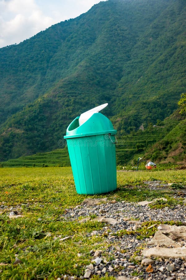 A Plastic Garbage Bin in the Middle of a Green Meadow with Mountains in ...