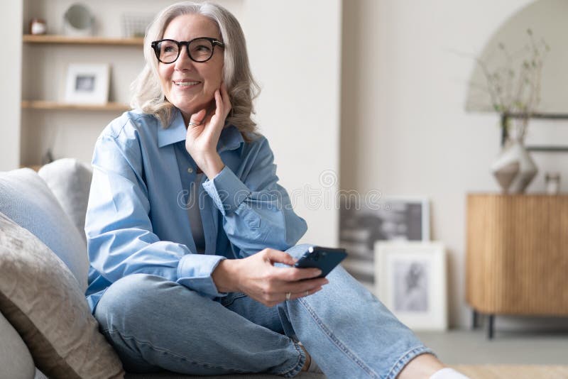 Pleasant Mature Lady Resting On Couch Using Applications On Smartphone
