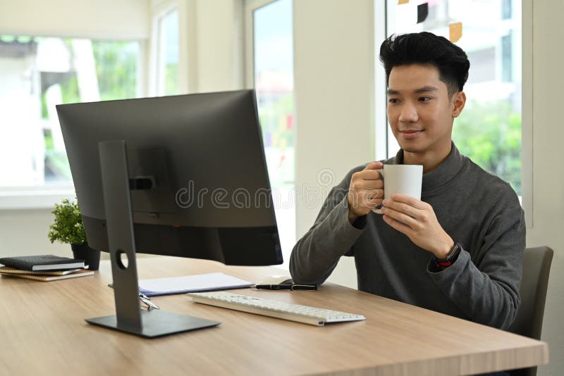 Pleasant Young Asian Man Freelancer Drinking Hot Coffee and Looking at ...
