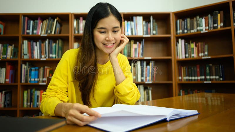 Pleased Female Student Reading Book in a Library for Studying and ...