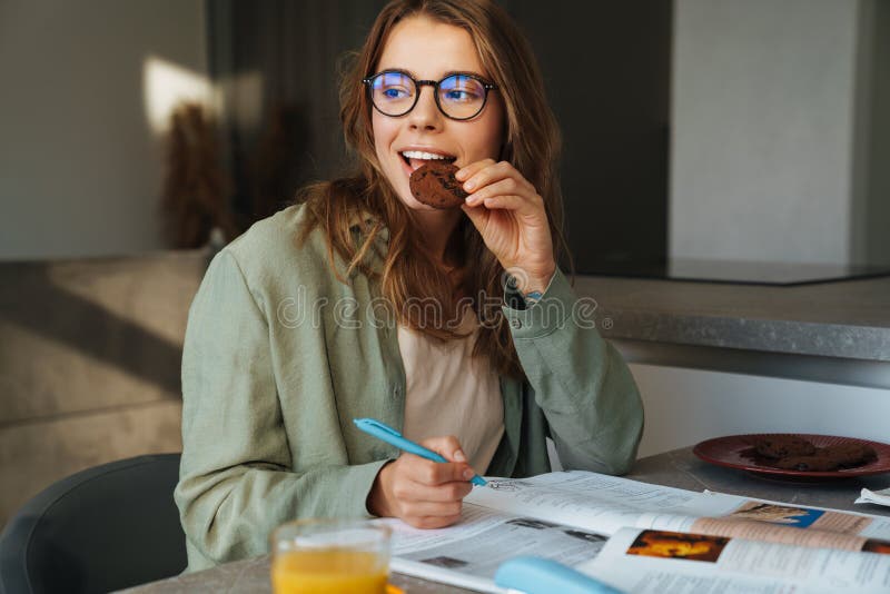 Pleased Student Woman Eating Cookie while Doing Homework at Home Stock ...