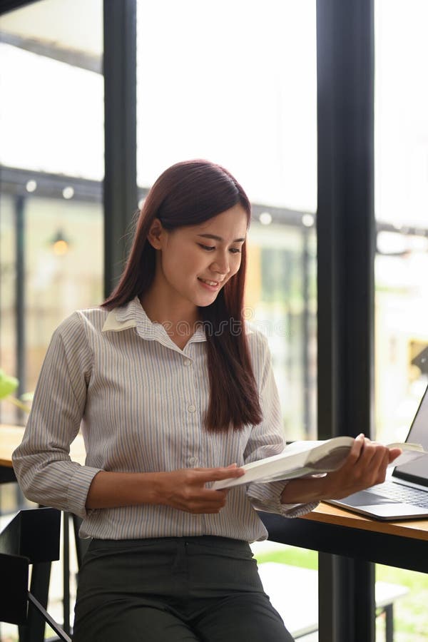 Pleased Young Asian Woman Resting from Work and Reading Book Stock ...