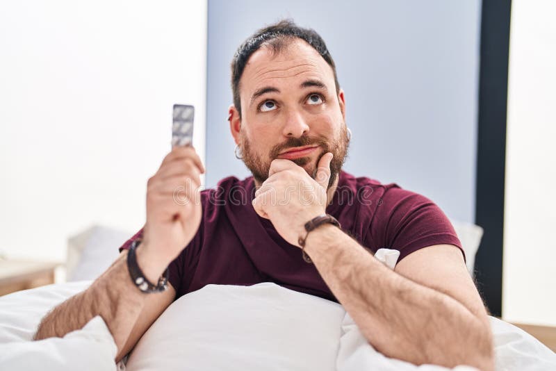 Plus Size Hispanic Man with Beard in the Bed Holding Pills Serious Face ...