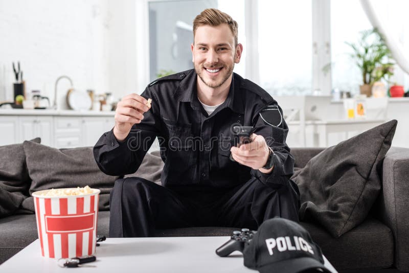 Police Officer Sitting on Couch, Holding Remote Control and Stock Photo ...