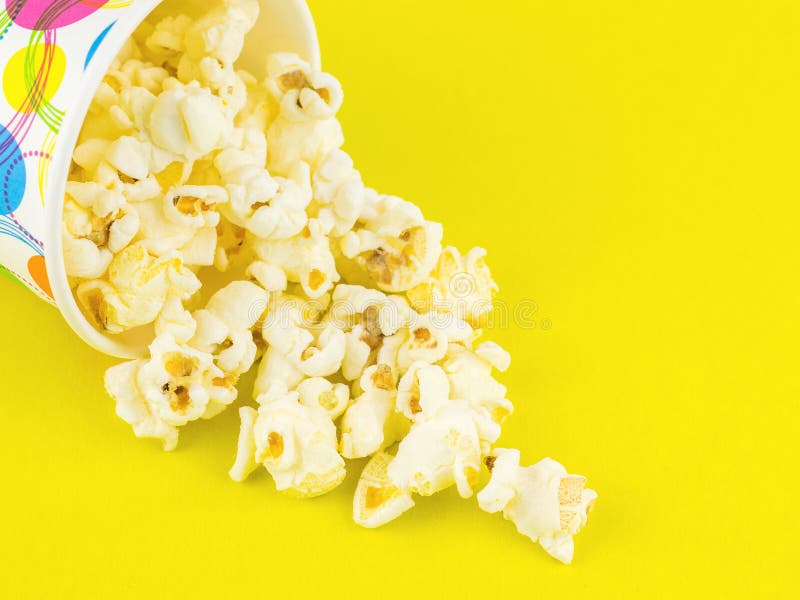 Popcorn is Poured from a Multi-colored Paper Cup on a Yellow Table ...