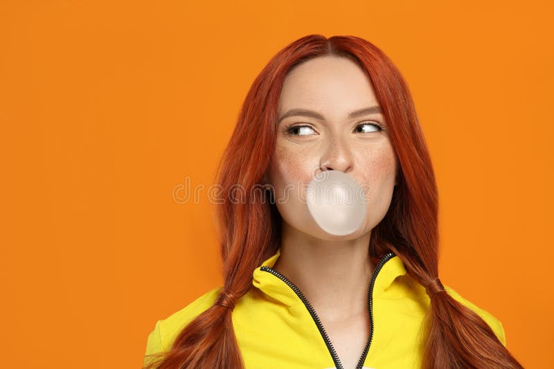Portrait Of Beautiful Woman Blowing Bubble Gum On Orange Background