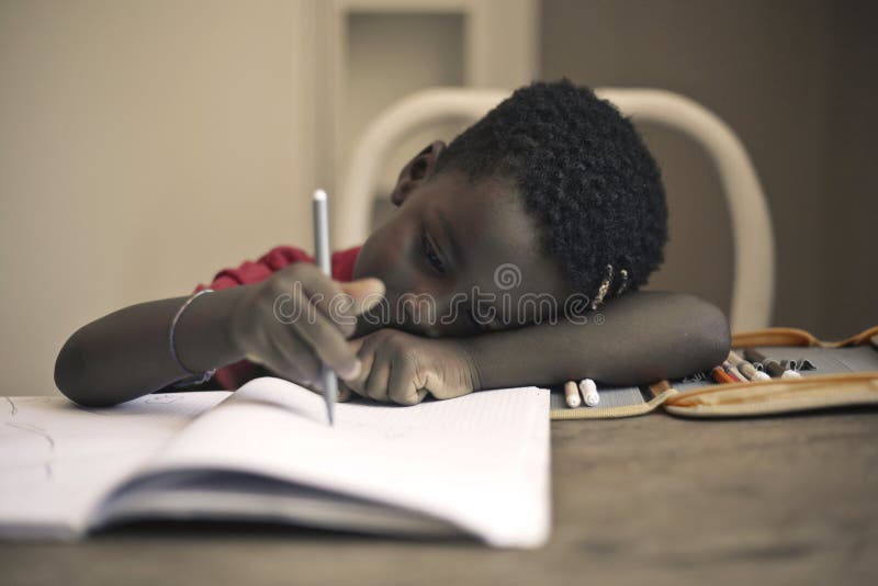 Portrait of a Bored Black Kid Writing in His Textbook while Lying on ...