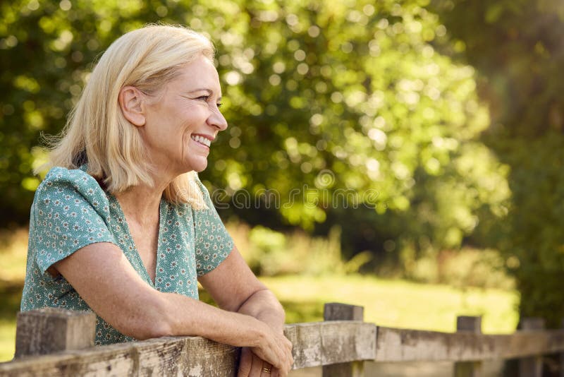 Portrait Of Casually Dressed Mature Or Senior Woman Leaning On Fence On