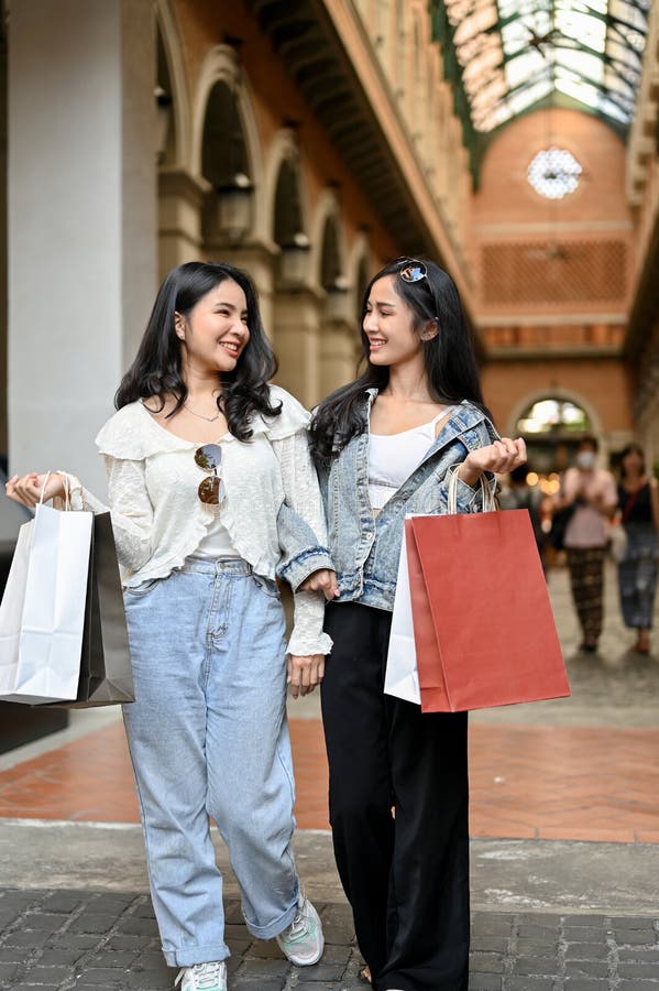 Asian Female Friends With Their Shopping Bags Sitting On The Street In