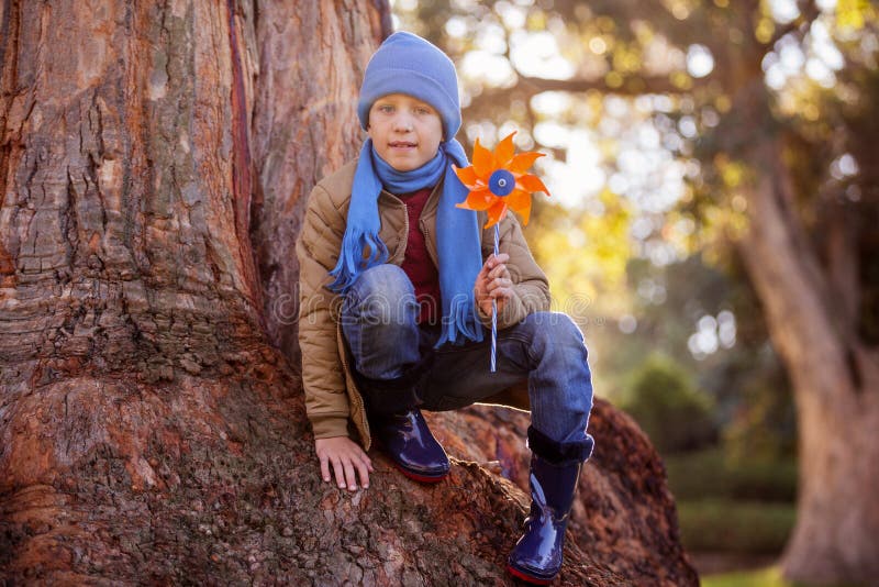 Portrait of Cute Boy Holding Pinwheel while Crouching on Tree Trunk ...