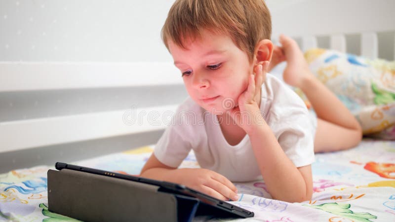 Portrait of Cute Smiling Little Boy Lying in Bed and Watching Video on ...