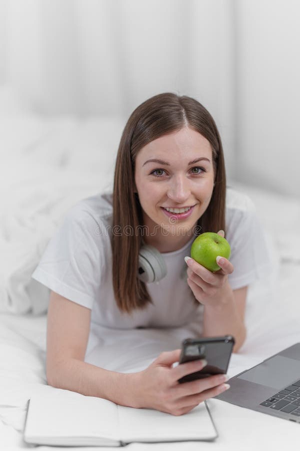 Portrait Of Good Healthy Woman Eating Green Apple And Resting In Bed At