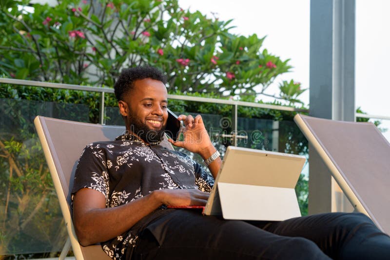 African Man Relaxing Outdoors while Using Laptop Computer and Mobile ...