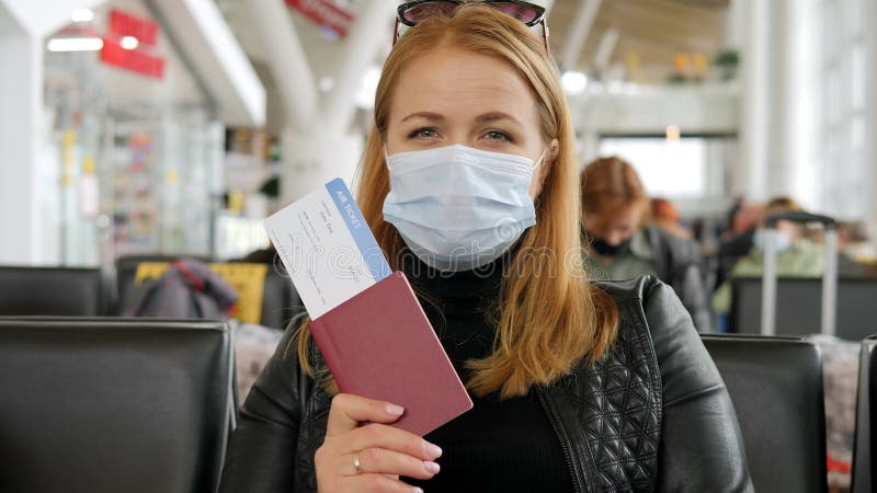 A Woman In A Medical Mask At The Airport With A Passport And A Plane