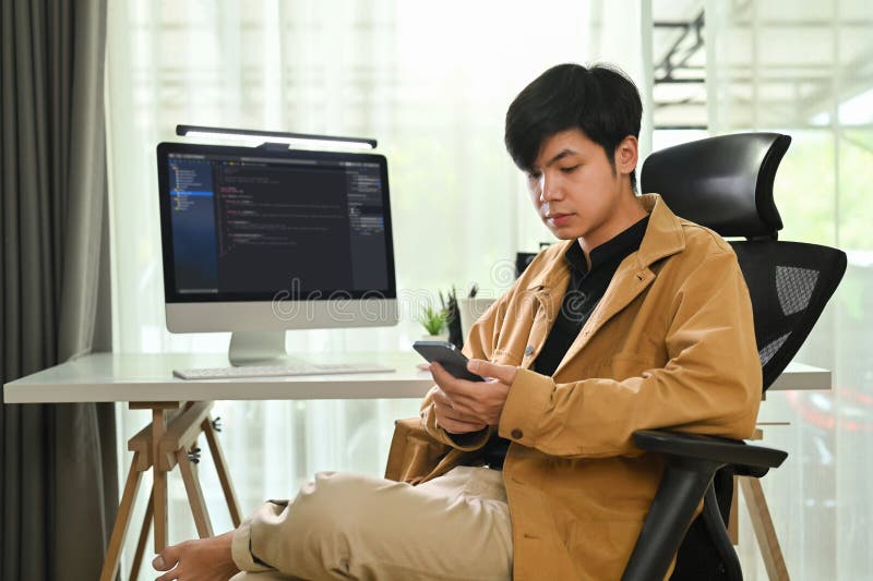 Portrait Of Male Programmer Sitting In Front Of Computer Monitor With Programming Code And Using