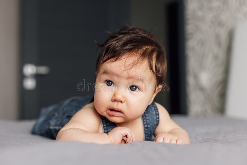 Portrait of Pretty Baby Wearing Denim Romper Lying on Gray Blanket at ... Portrait of Pretty Baby Wearing Denim Romper Lying on Gray Blanket at ...