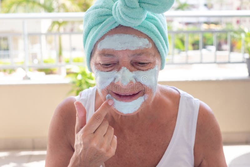 Portrait Of A Pretty Smiling Senior Woman Applying A Cleansing Mask On