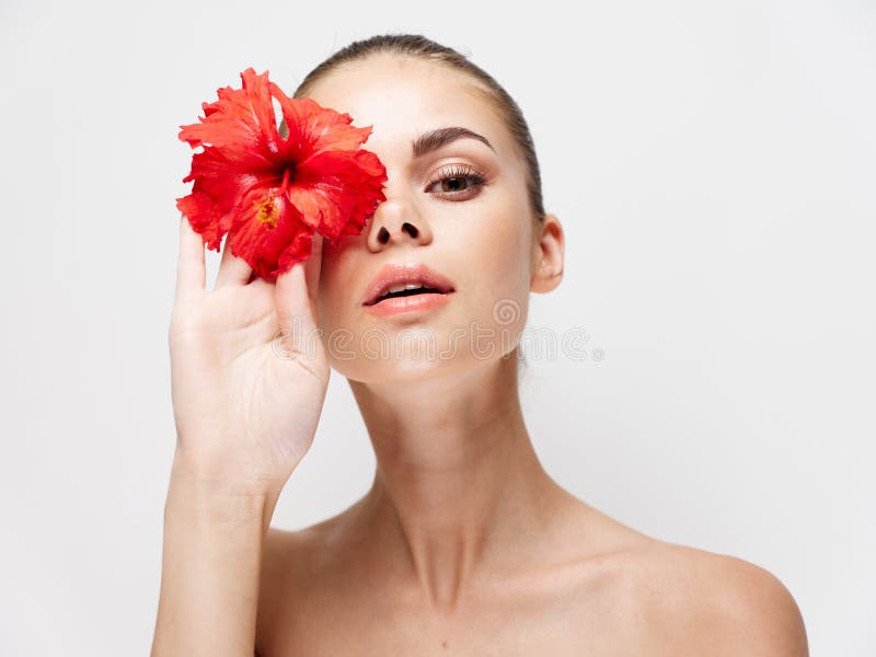 Portrait Of Pretty Woman With Red Flower Near Face On Light Background