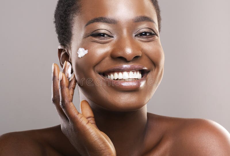 Portrait Of Smiling Black Woman Applying Moisturizing Cream On Face