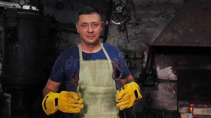 Portrait of a Smiling Blacksmith with Metal Tools in His Hands in a ...