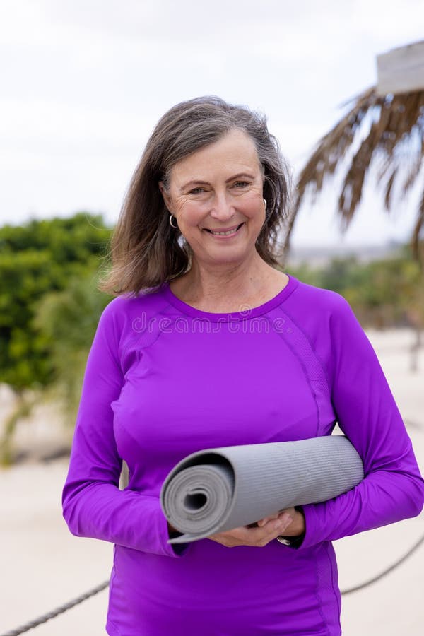 Portrait Of Smiling Caucasian Senior Woman With Exercise Mat Standing At Tourist Resort Stock
