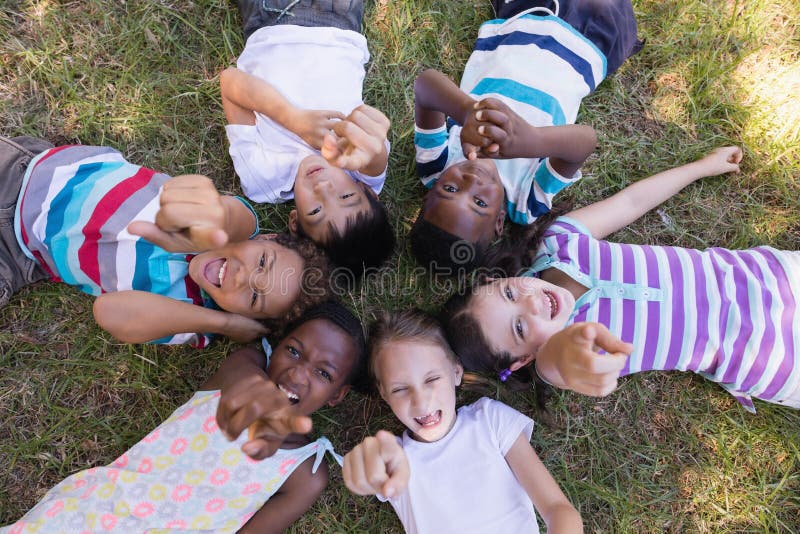 Portrait of Smiling Friends Pointing Up while Lying on Grassy Field ...