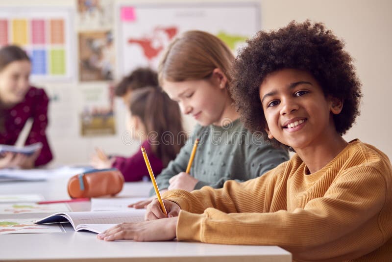 Smiling Male Elementary School Teacher Working at Desk in Classroom ...