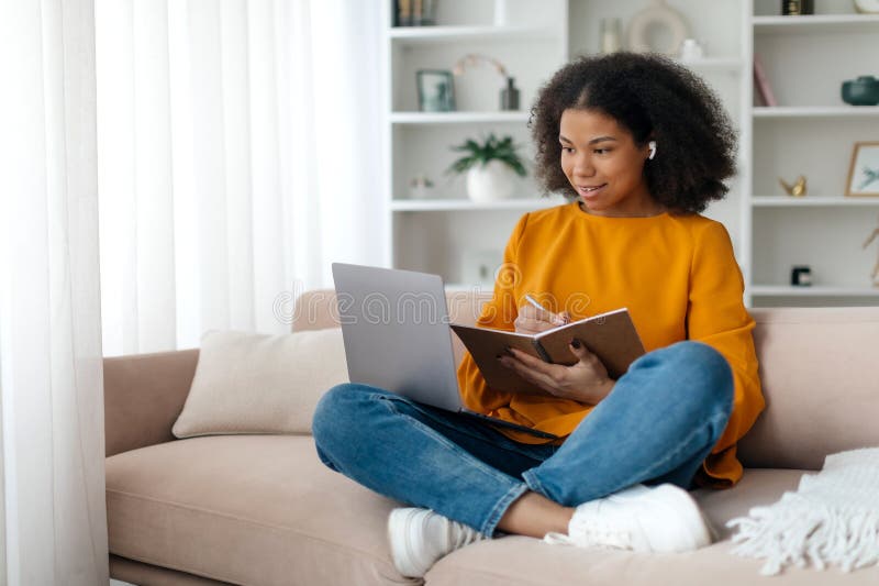 Portrait of Smiling Woman Sitting on Sofa, Using Laptop and Writing in ...