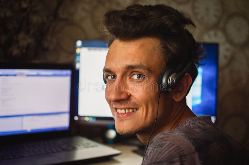 Portrait of a Smiling Young Man in Headphones Working on Two Computers ...