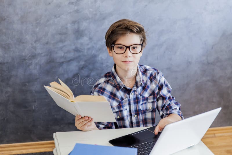 Teen Boy Reading Book and Using Laptop in Room Stock Image - Image of ...